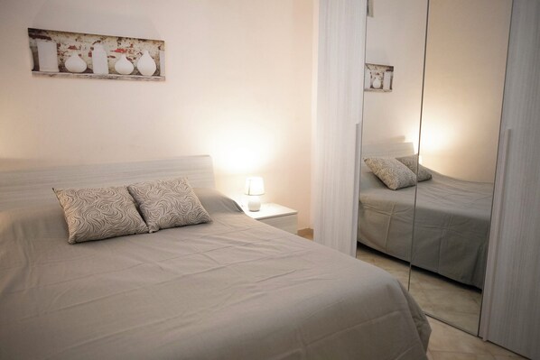 Quarto com cama, mesa de cabeceira e espelho.