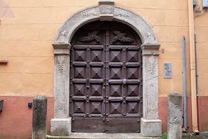 Uma porta de madeira grande e elaborada, com um arco de pedra, embutida em um edifício com parede amarela.