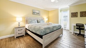 Quarto com cama, mesas de cabeceira, escrivaninha e ventilador de teto.