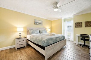 Quarto com cama, mesas de cabeceira, escrivaninha e ventilador de teto.