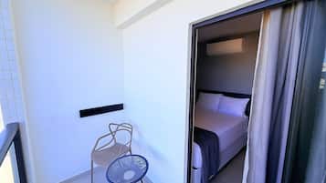 Quarto de hotel com cama, ar-condicionado fixado na parede, uma cadeira e janela com cortinas.