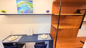 Uma área de refeições com uma mesa posta para dois, um cardápio e uma pintura sobre a mesa.