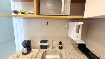 Cozinha compacta com micro-ondas, cafeteira, pia e dispensador de água.