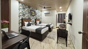 Quarto de hotel moderno com duas camas, uma escrivaninha com um laptop, uma cadeira, um ventilador de teto e uma TV fixada na parede.