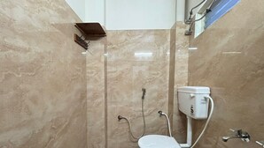 Casa de banho com sanita, chuveiro e um pequeno armário sobre a sanita.