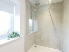 Um banheiro moderno com box de vidro, banheira branca e janela com uma planta no parapeito.