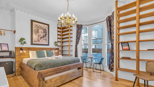 Quarto com cama de madeira, um candelabro, escrivaninha e vista para o exterior.
