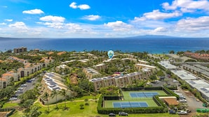 Vista aérea de uma área residencial costeira com vilas, uma quadra de tênis e vista para o oceano.