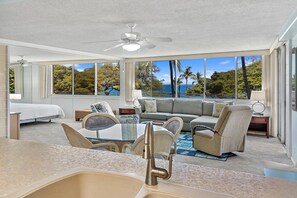 Uma sala de estar moderna com uma janela grande, um ventilador de teto e um espaço de jantar com mesa e cadeiras.