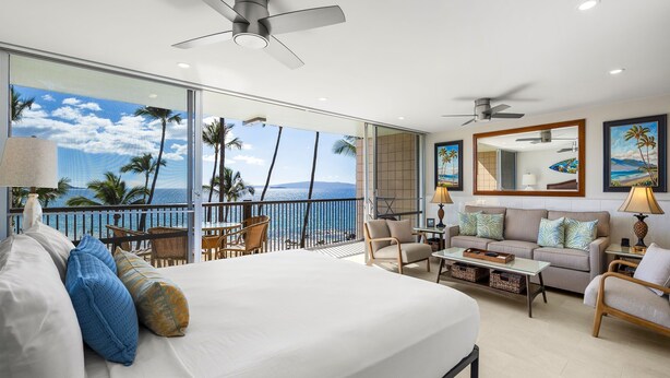 Um quarto espaçoso com uma cama grande, varanda com vista para o mar e um espaço de estar com sofá e cadeiras.