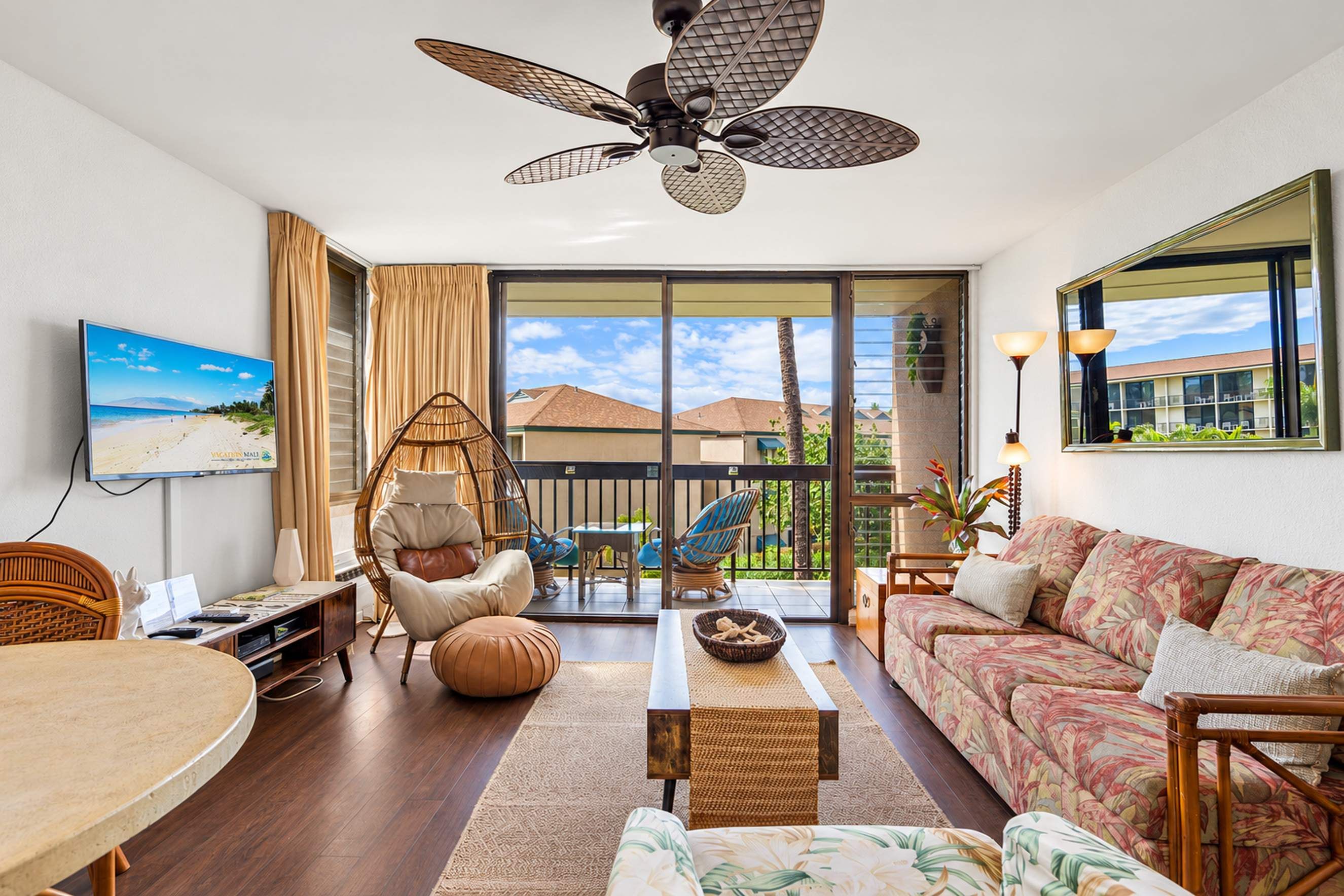 Uma sala de estar espaçosa com ventilador de teto, televisão e sofá com estampa floral.