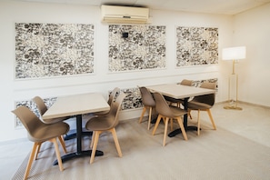 Quarto de hotel com área de refeições, incluindo mesa, cadeiras, luminária de chão e painel decorativo com padrão floral.