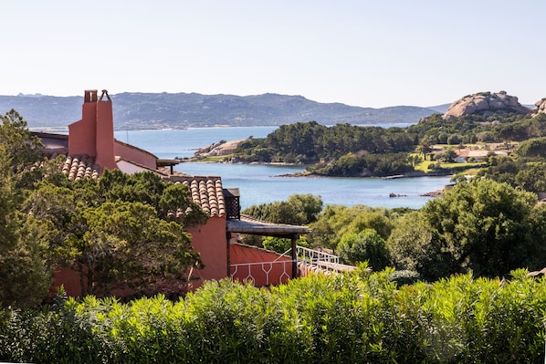 Um edifício costeiro com fachada vermelha, chaminé e vista para o mar e colinas.