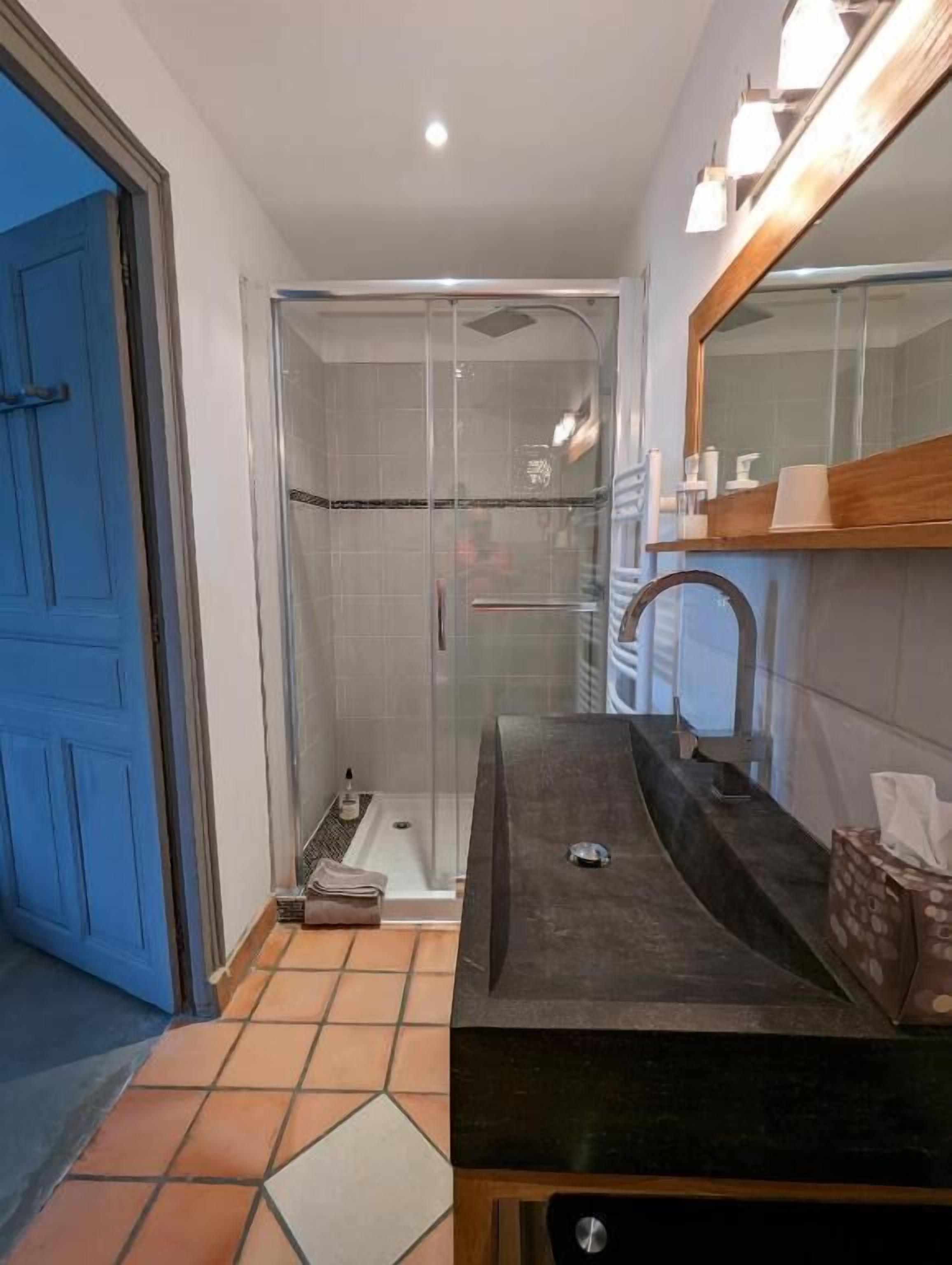 Casa de banho com cabine de duche em vidro, lavatório com espelho e barra de toalhas.