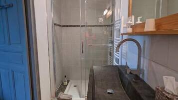 Casa de banho com cabine de duche em vidro, lavatório com espelho e barra de toalhas.