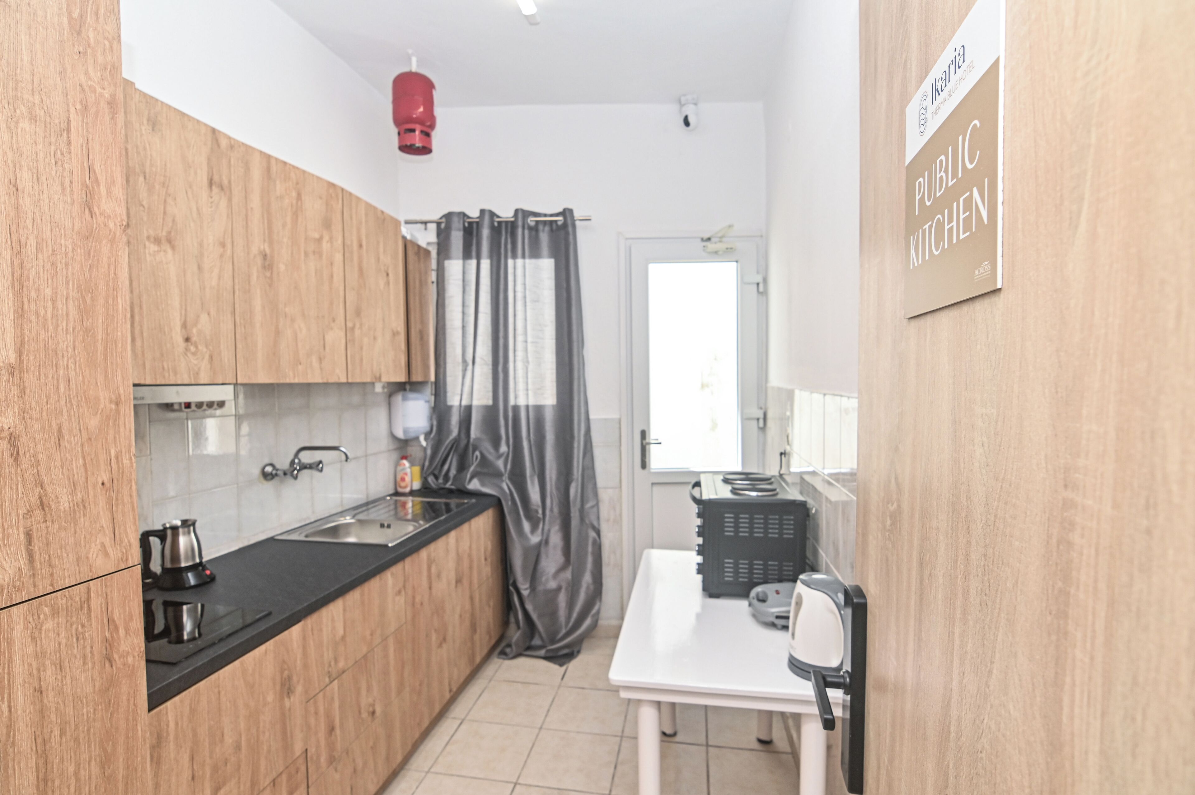 Uma cozinha compacta com armários de madeira, bancada preta, pia e uma mesa com chaleira.