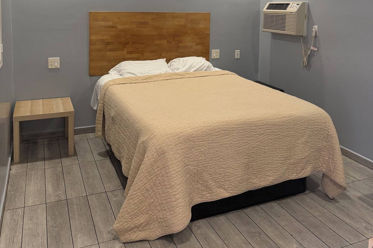 Quarto com cama, mesa de cabeceira, cabeceira de madeira, ar-condicionado fixado na parede e luz no teto.