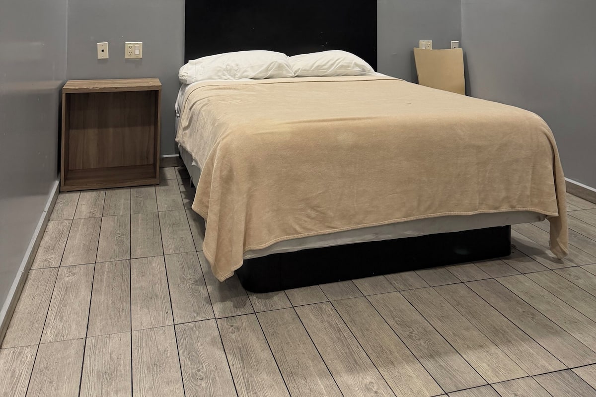 Um quarto com cama, mesa de cabeceira, cadeira e armário de madeira.