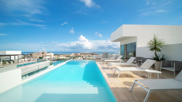 Uma piscina no terraço com água azul cristalina, cadeiras de sol brancas e vista para o horizonte da cidade.