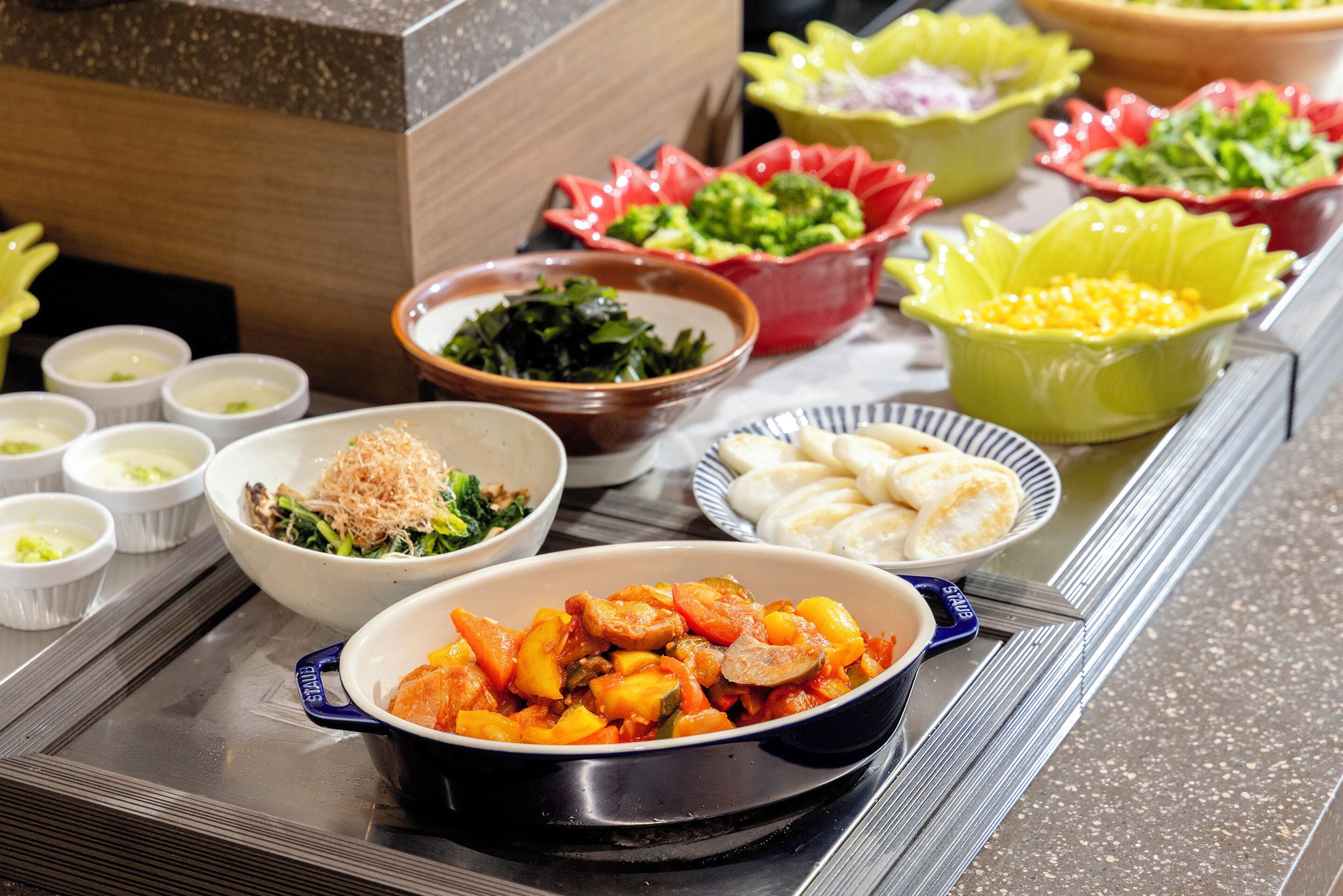 Buffet com diversos pratos, incluindo legumes, frutos do mar e dumplings.