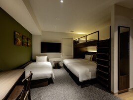 Quarto de hotel com beliches, uma escrivaninha, uma cadeira, televisão e obras de arte na parede.