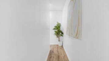Um corredor com paredes brancas, piso de madeira e um vaso com planta.