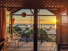 Um deck de madeira com cadeiras de frente para uma praia ao pôr do sol.
