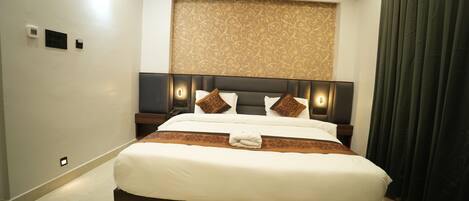 Quarto de hotel moderno com uma cama grande, cabeceira com iluminação integrada, painel decorativo na parede e cortina escura.