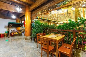 Interior rústico de madeira com piso de pedra, mesas e cadeiras de madeira, e plantas em vasos.
