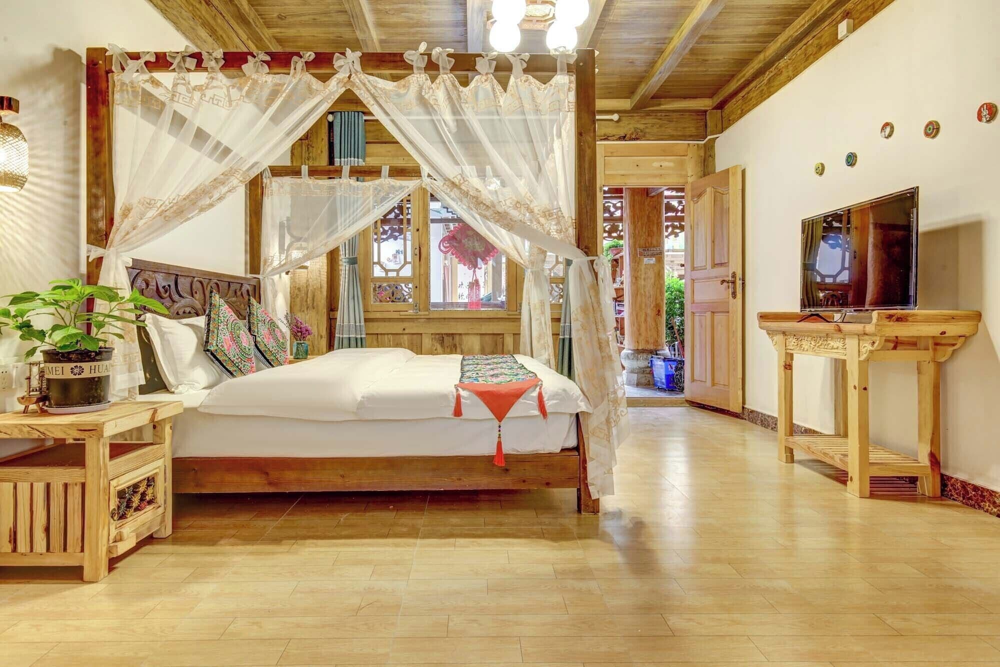 Quarto com cama de dossel, mesa de cabeceira com planta, televisão sobre suporte de madeira e janela com vista para o exterior.