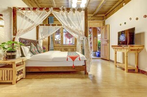 Quarto com cama de dossel, mesa de cabeceira com planta, televisão sobre suporte de madeira e janela com vista para o exterior.