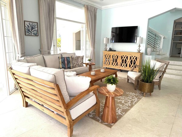 Uma sala de estar moderna com sofá, mesa de centro, cadeiras, televisão e um armário de madeira.