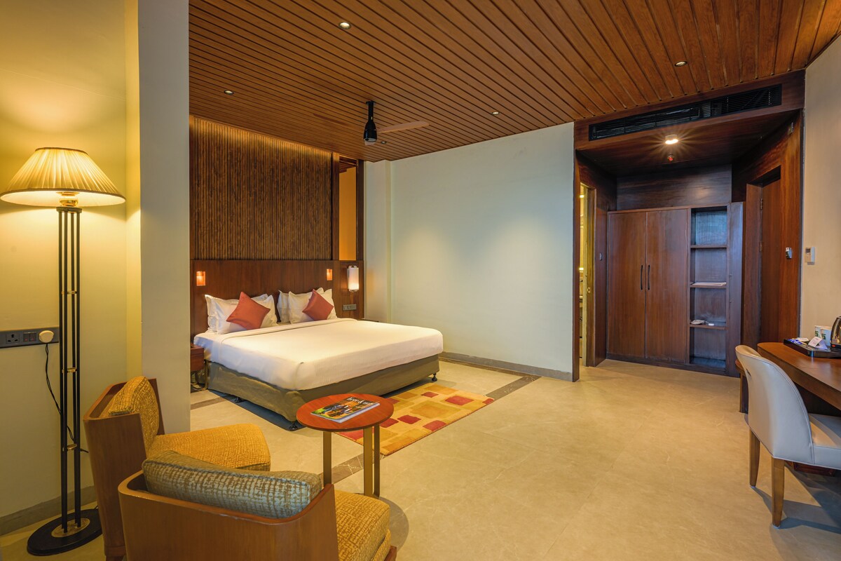 Quarto de hotel com cama, abajur, cadeira, escrivaninha e guarda-roupa.