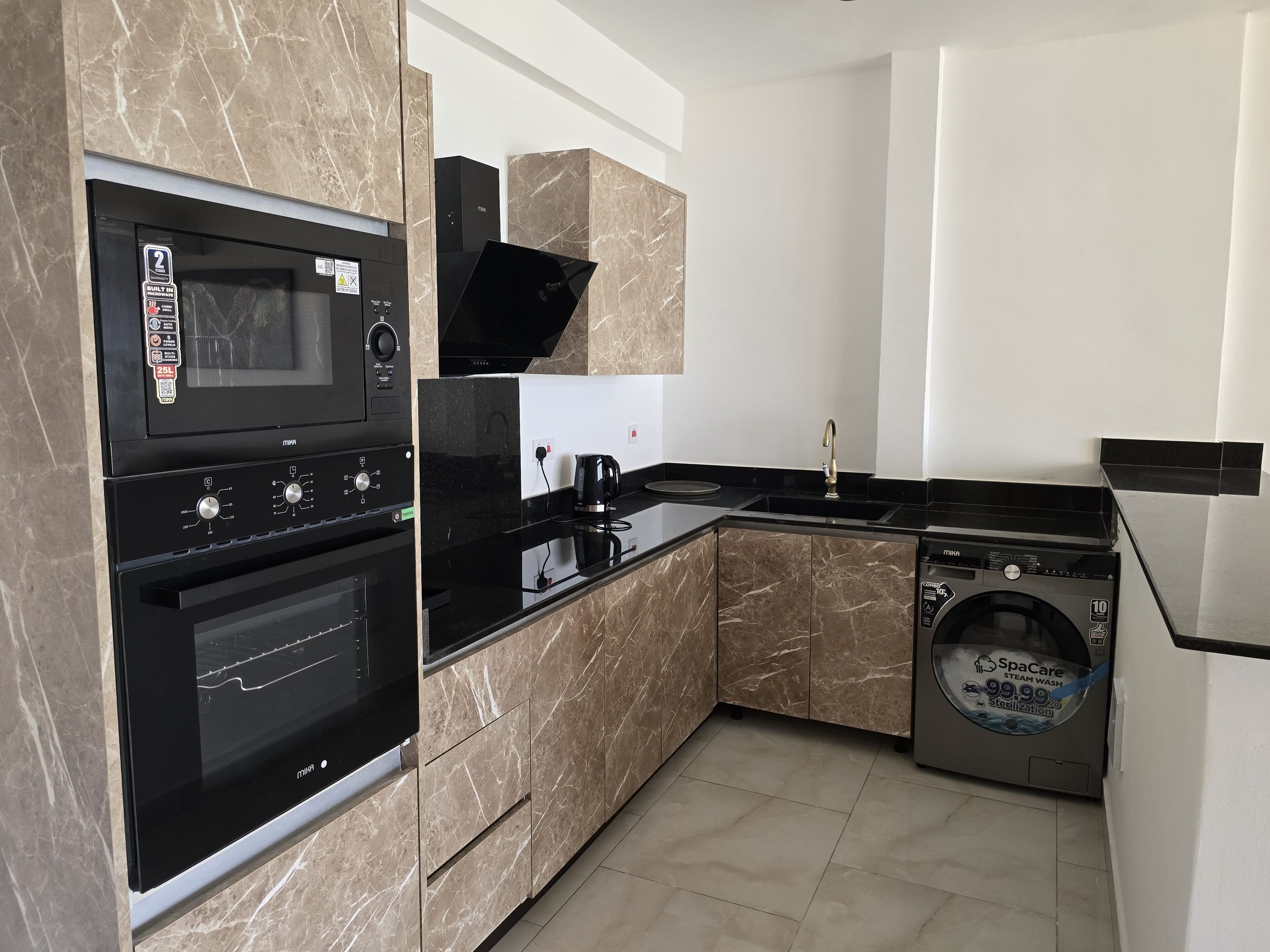 Uma cozinha moderna com forno embutido, micro-ondas e lava-louças, com bancadas e armários de mármore.