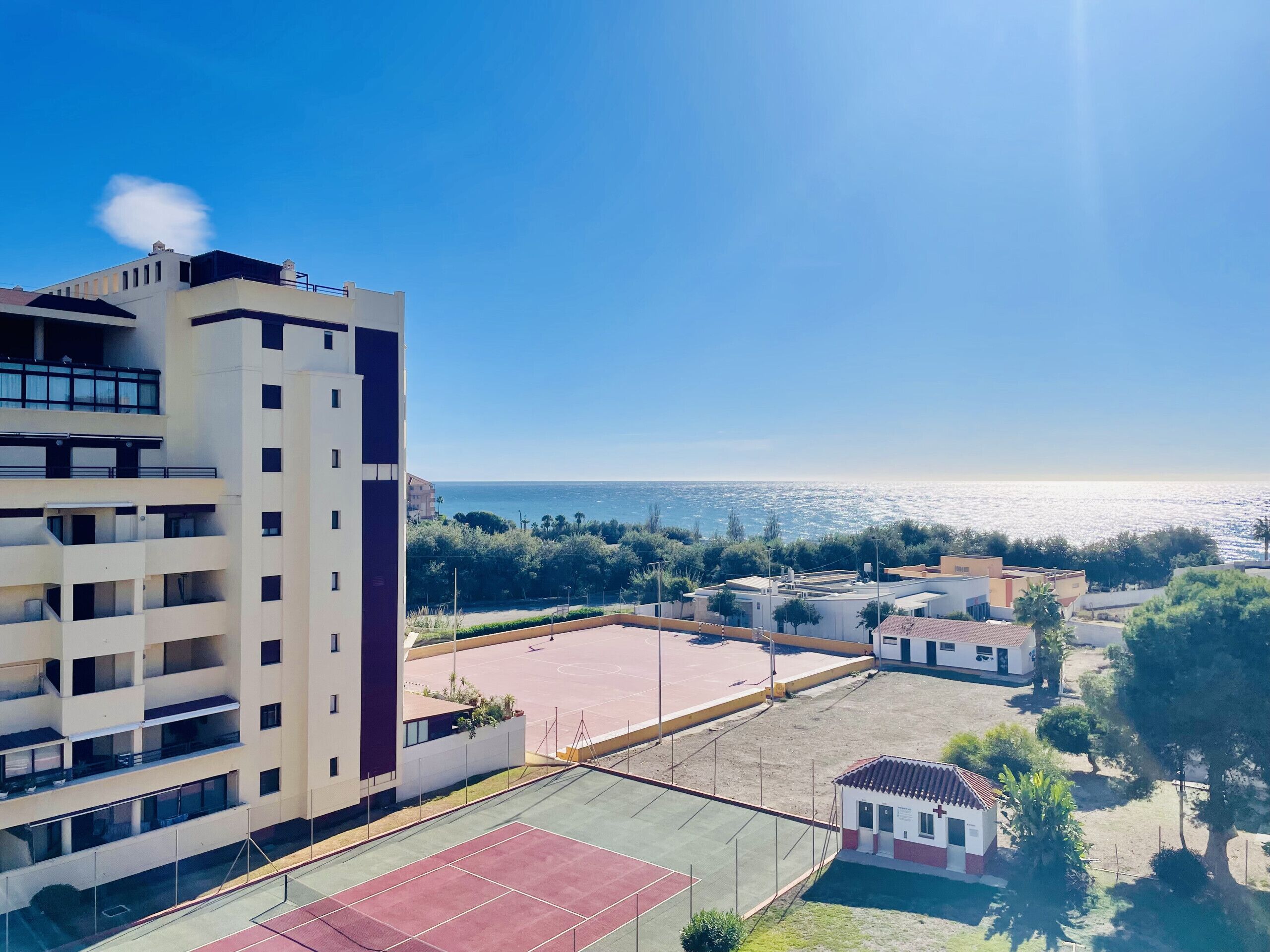 Um edifício de vários andares com terraço no telhado, quadra de tênis e uma pequena capela.