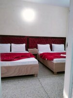 Quarto de hotel com duas camas, cada uma com um cobertor vermelho, uma cabeceira de madeira e uma pequena mesa de cabeceira com abajur.