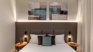 Quarto de hotel moderno com uma cama grande, duas mesas de cabeceira e arte abstrata na parede.