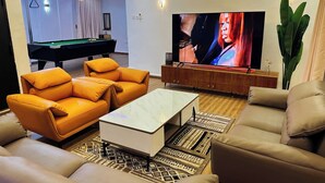 Uma sala de estar moderna com mesa de bilhar, assentos confortáveis, TV de tela plana e iluminação ambiente.
