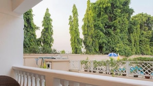Varanda com móveis de vime, balaustrada branca e vista para árvores e uma piscina.