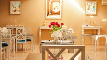 Uma sala de jantar com móveis brancos, um vaso com flores vermelhas e quadros nas paredes.