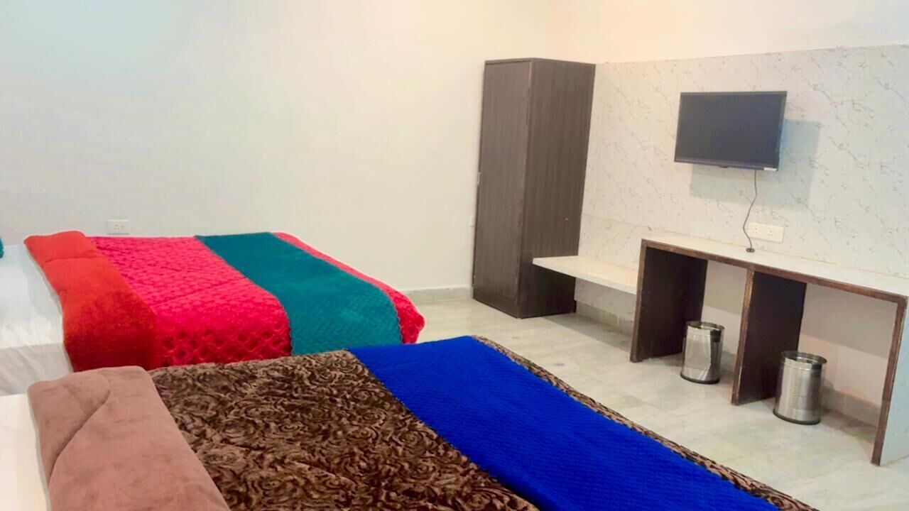 Quarto com duas camas, televisão fixada na parede, armário e uma mesinha com lixeiras.