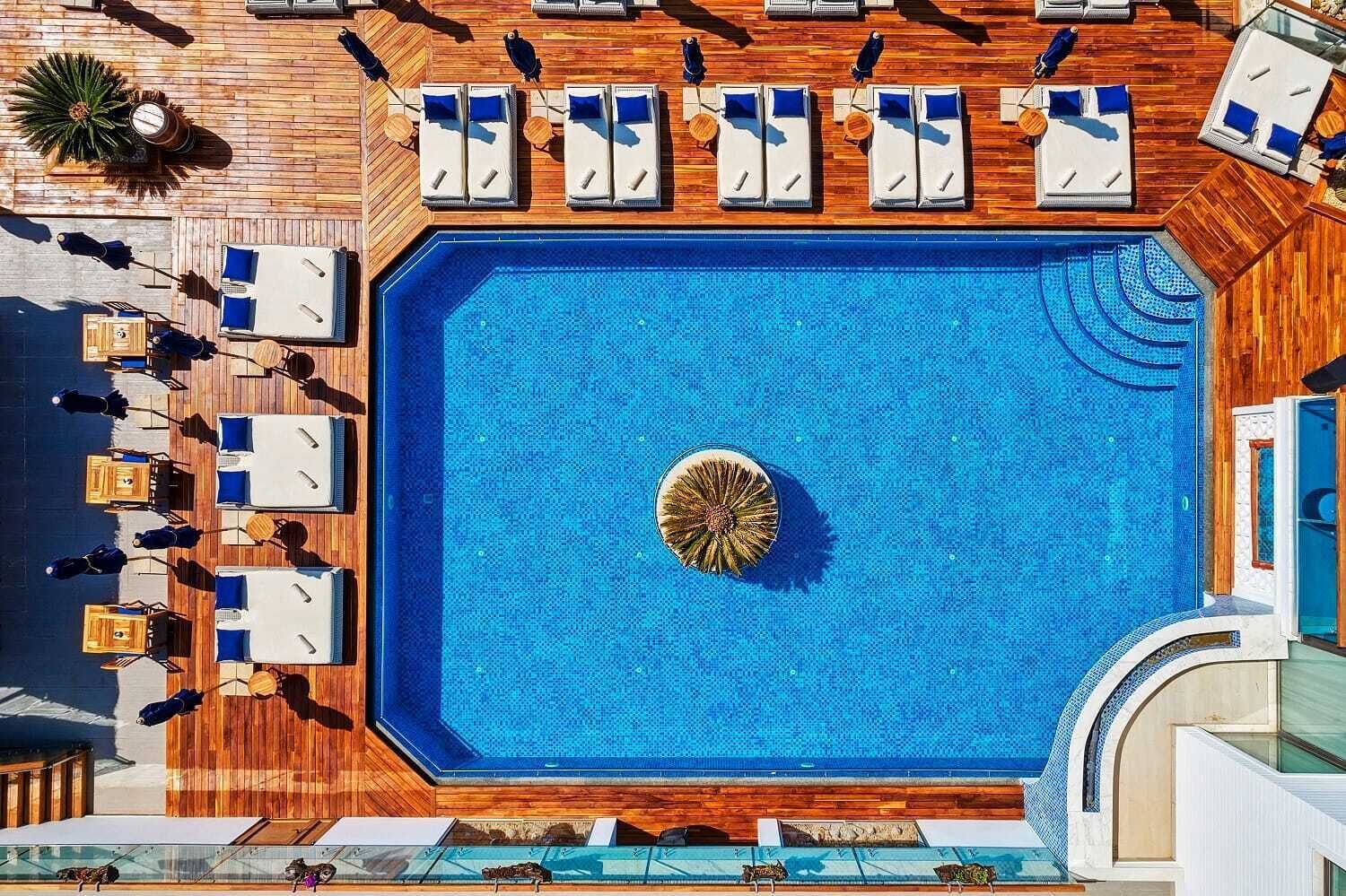 Vista aérea de uma área de piscina com espreguiçadeiras e um elemento decorativo central.
