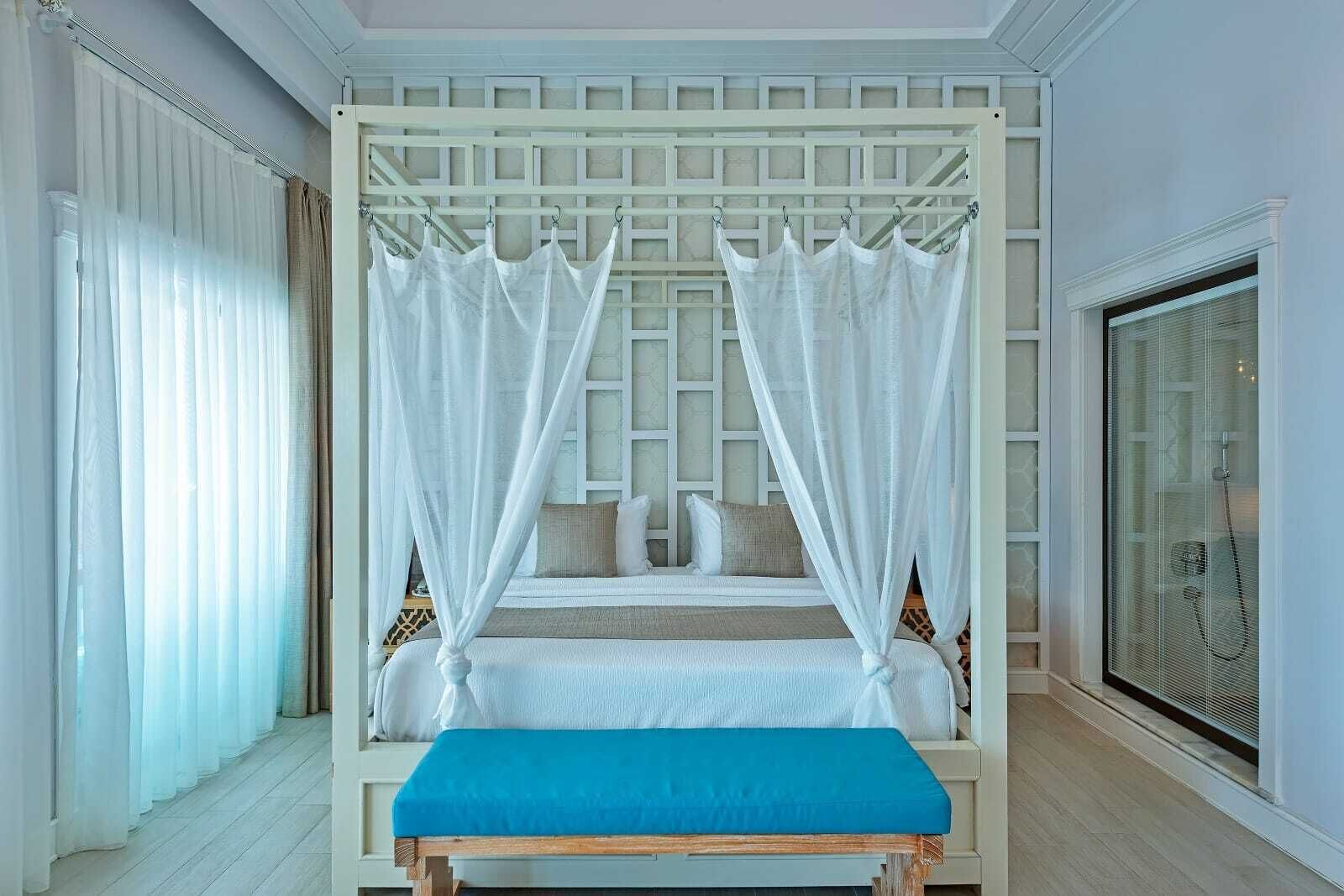 Quarto com cama de dossel, um banco e vista para a área do chuveiro.
