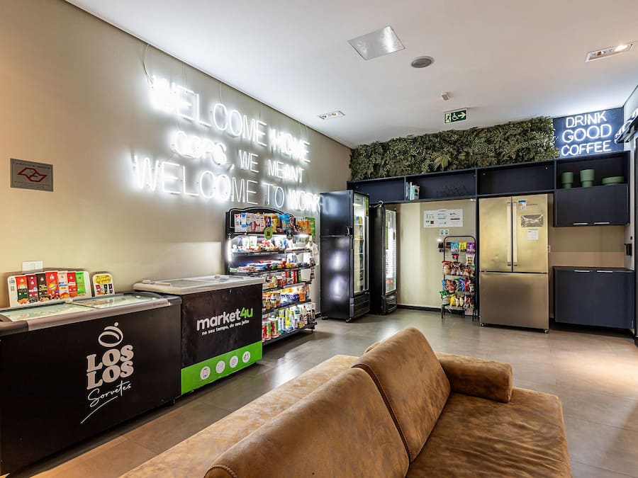 Um lobby moderno com uma placa de 'Welcome', uma placa de 'Drink Good Coffee', um quiosque 'Market 4U' e uma área de kitchenette.