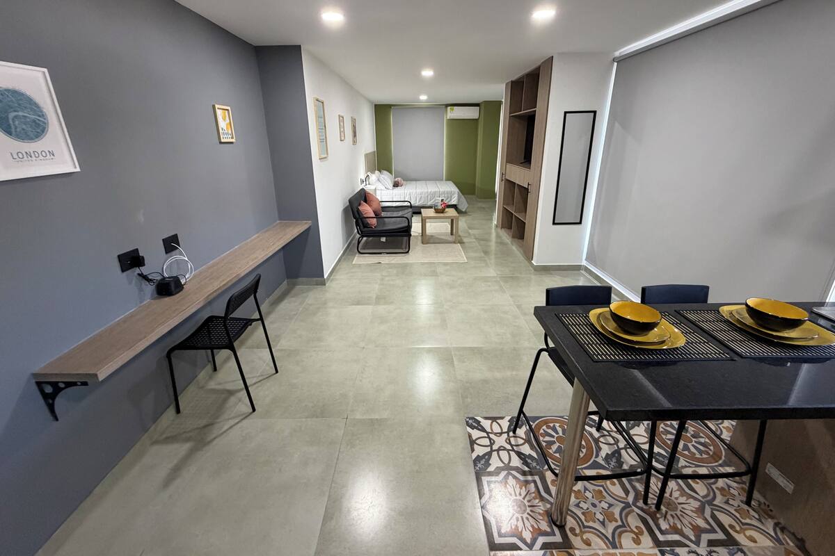 Quarto de hotel moderno com cama, escrivaninha, mesa de jantar e cadeiras, e um pequeno espaço para sentar.
