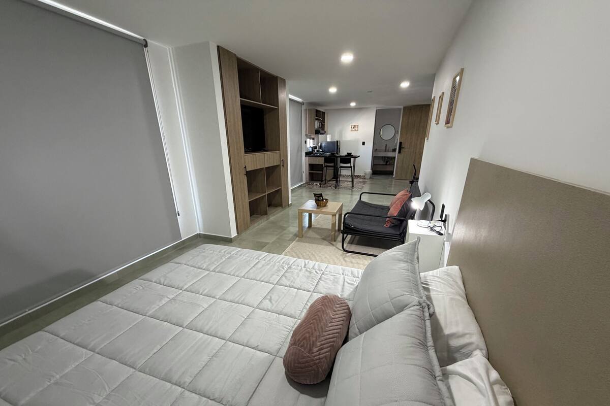Quarto com cama, escrivaninha e uma kitchenette ao fundo.