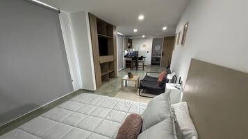 Quarto com cama, escrivaninha e uma kitchenette ao fundo.