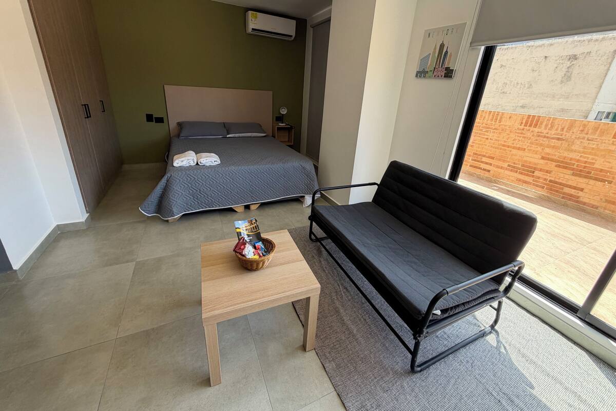 Quarto moderno com cama, sofá, uma mesinha com cesta e janela com vista.