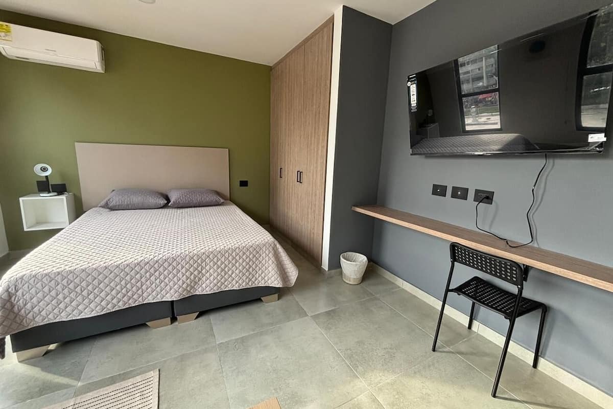 Quarto com cama, escrivaninha, televisão e guarda-roupa.