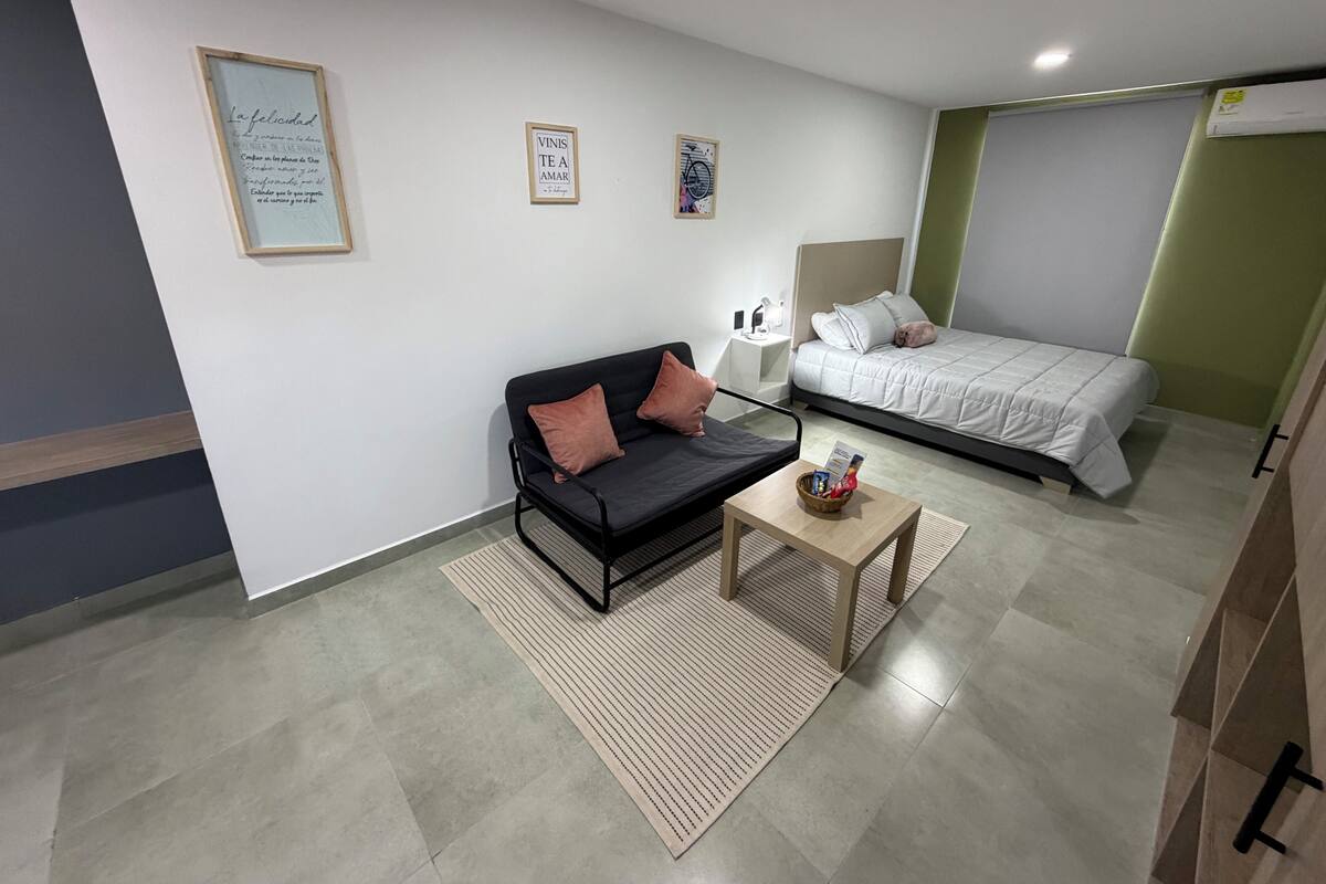Quarto moderno com sofá preto, uma mesinha, cama e parede com citações emolduradas.